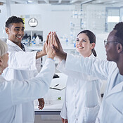 Diverse group of happy scientists giving each other a high give to celebrate their success while ...