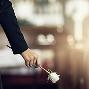 Flower, funeral and hand holding rose in mourning at death ceremony ...