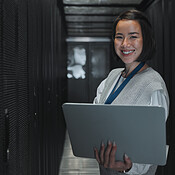 Woman with laptop, server room and information technology, smile in ...