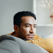 Thinking, memory and sad asian man on a sofa with nostalgia, depression or grief in his home ...