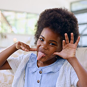 Funny, face and girl child with tongue out on a sofa for fun, playing or goofy personality at ...