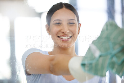A young happy mixed race domestic worker using a cloth on a window. One ...