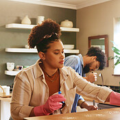Woman, cloth and cleaning with spray by kitchen counter in home with ...