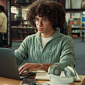 Student, man and typing on laptop in library for learning, education or ...