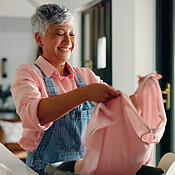 Happy old woman, cleaning and folding laundry in home for housekeeping ...
