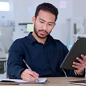 Web developer reading digital tablet, writing notes and thinking of ...